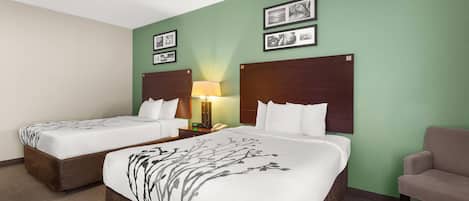 Quarto de hotel com duas camas, um sofá, uma luminária e quadros nas paredes.