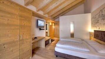 Quarto com piso de madeira, uma cama, televisão e escrivaninha.