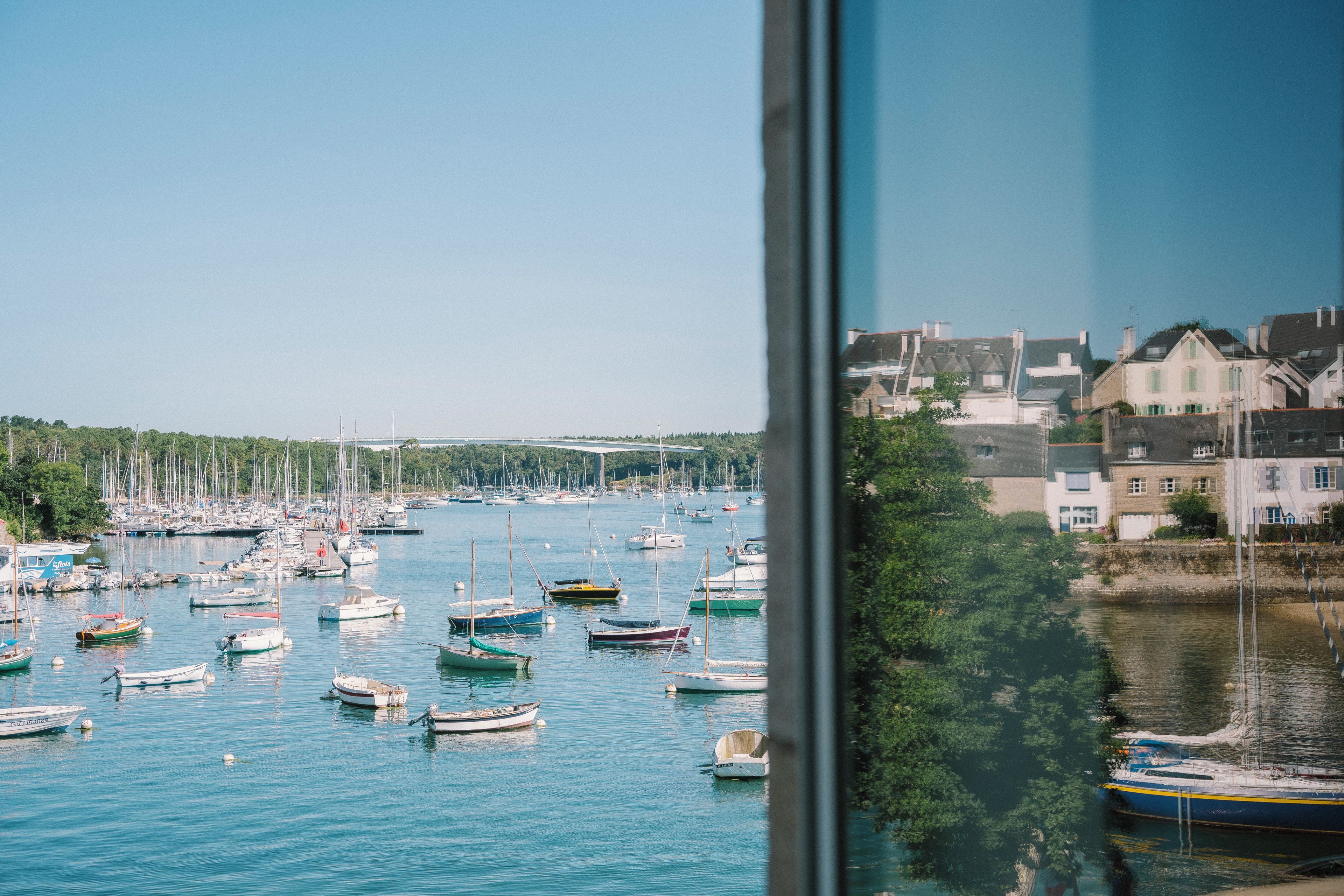 Marina com diversos barcos atracados, céu claro e edifícios ao fundo.