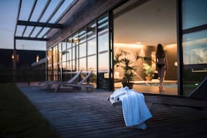 Exterior moderno de hotel com fachada de vidro, deck de madeira e cadeiras de descanso.