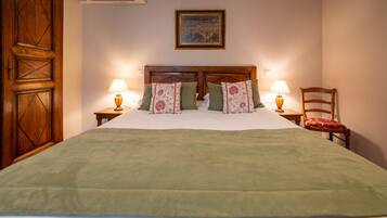 Uma cama bem arrumada com um cobertor verde, duas luminárias de cabeceira e uma cadeira de madeira.