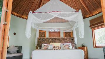 Quarto com cama de dossel, cabeceira de madeira e vista para o exterior.