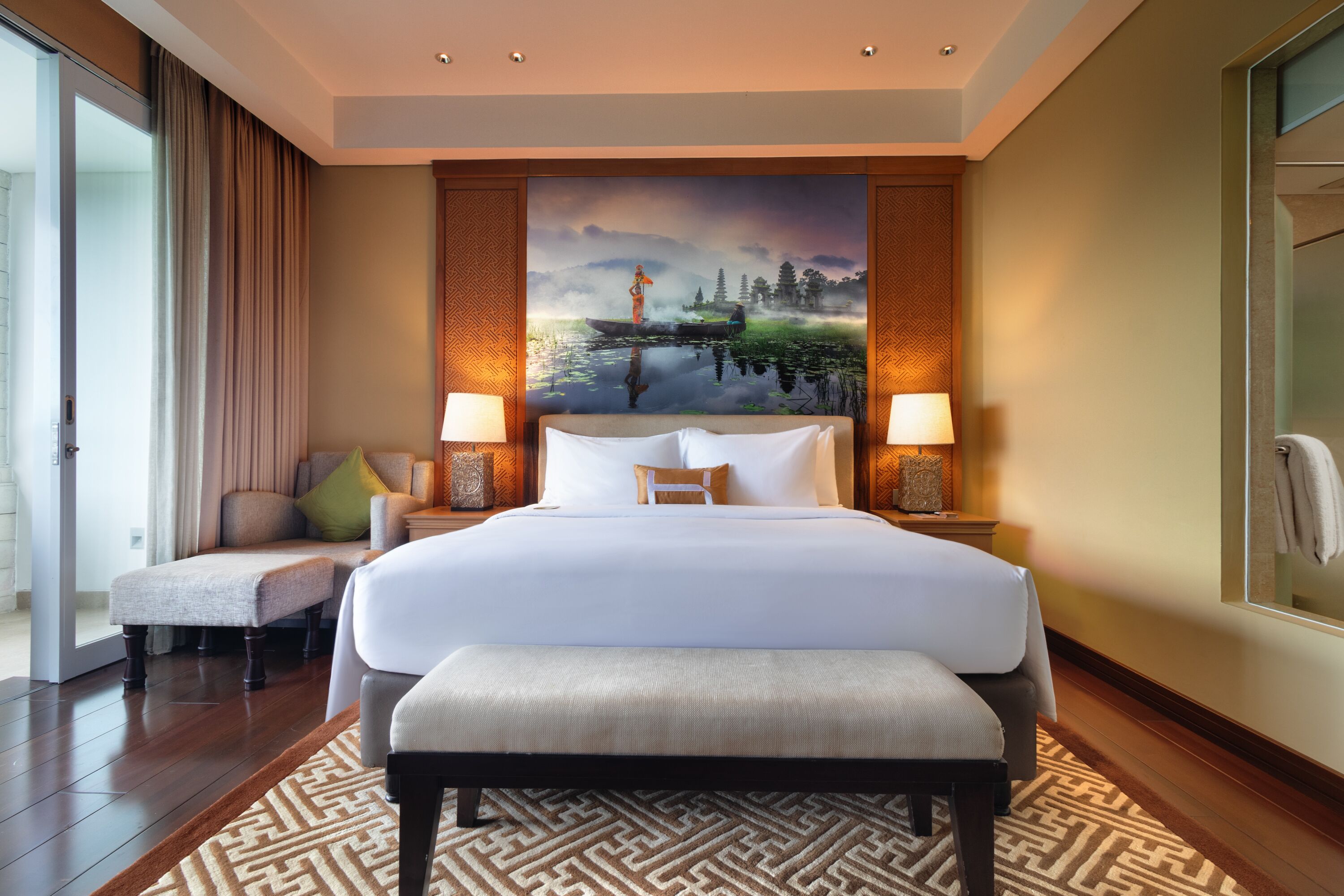 Quarto de hotel com uma cama grande, um banco, um sofá e um quadro na parede.