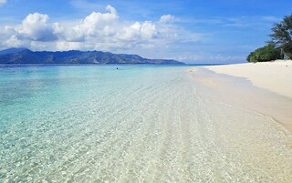Uma praia com águas turquesa cristalinas, areia branca e montanhas ao fundo.