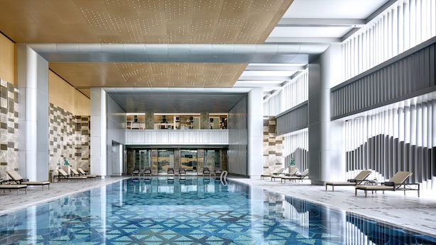 Uma piscina interior moderna com padrões geométricos em azulejos, espreguiçadeiras e um design arquitetônico contemporâneo.
