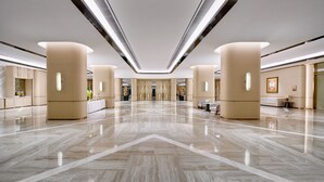 Um hall amplo com piso de mármore polido, pilares largos bege e design moderno no teto.