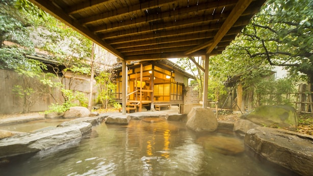 Uma onsen japonesa tradicional com estrutura de madeira e área de banho em pedra.