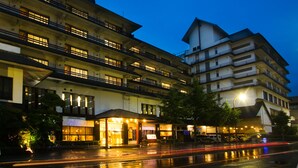 Um hotel com vários andares, varandas, entrada coberta e vista para a rua com reflexos no asfalto molhado.