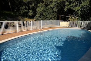 Piscina transparente com deck de madeira e cerca de metal branca.