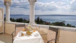 Mesa de varanda posta para o pequeno-almoço, com vista para a paisagem marítima e colinas ao longe.