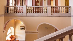 Um interior imponente com uma escadaria, um candelabro e uma varanda com balaustrada.
