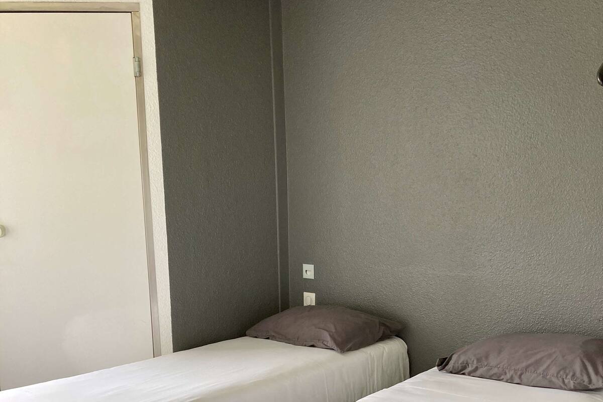 Um quarto com duas camas de solteiro, uma porta e um interruptor de luz na parede.