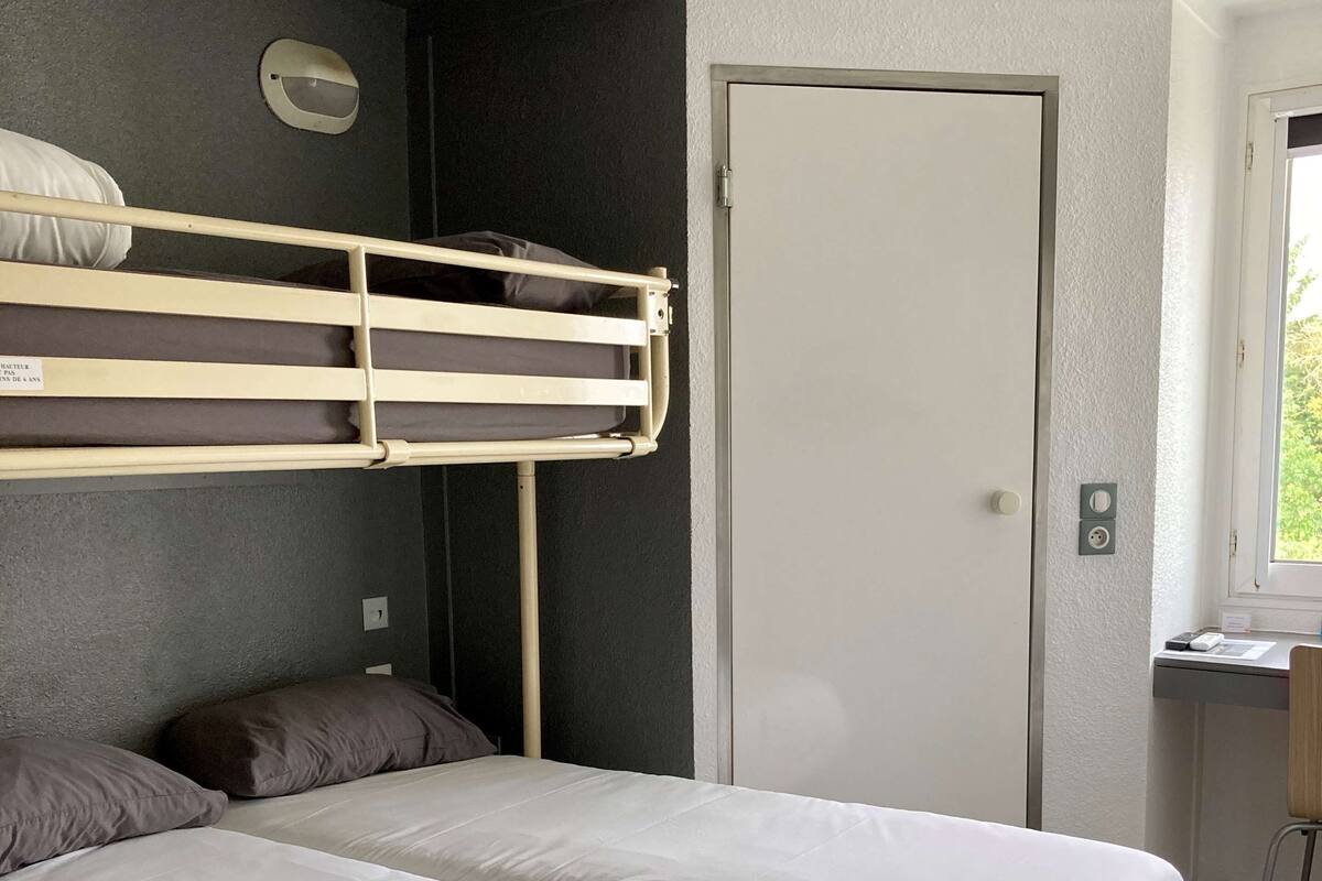 Quarto com duas camas, incluindo uma cama beliche, uma porta e uma janela.