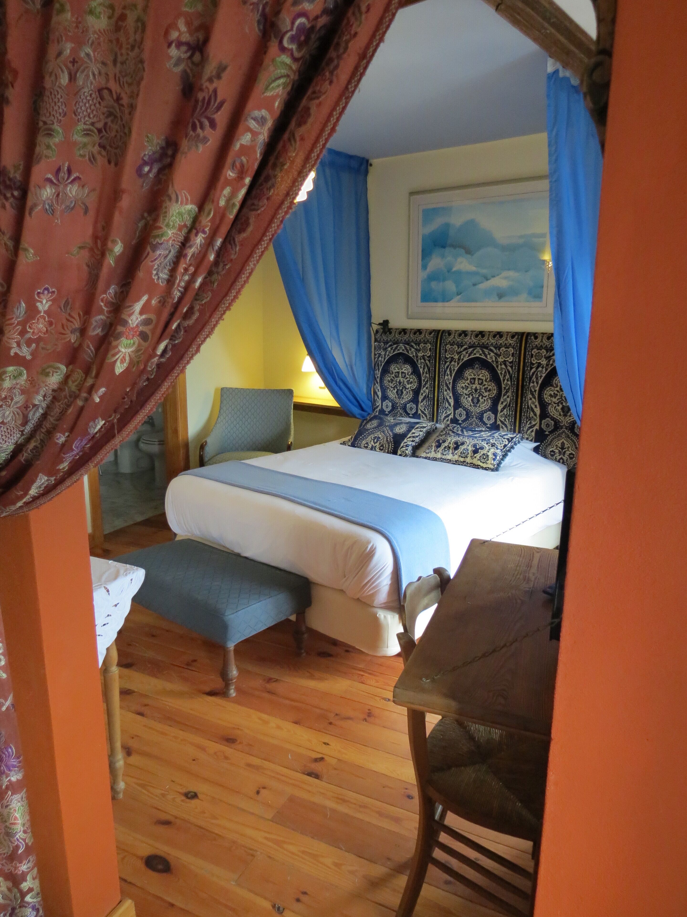 Um quarto com cama, cadeira, mesa e piso de madeira.