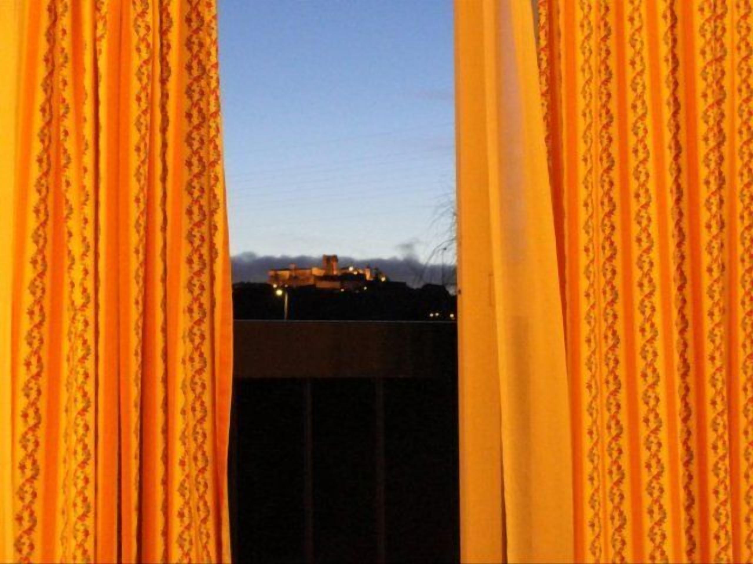 Visão através de cortinas, com um edifício distante e céu claro.