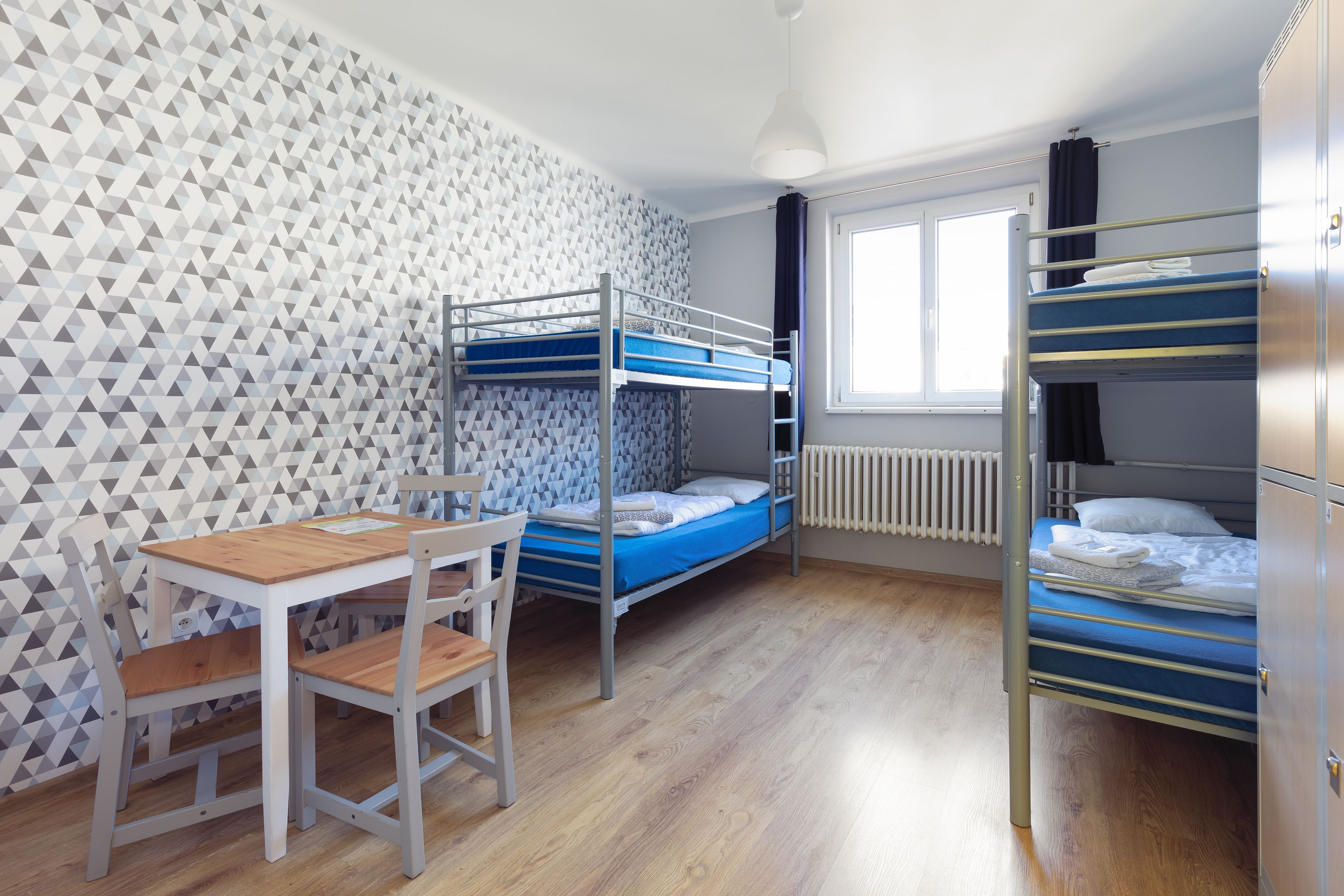 Quarto pequeno com beliches, uma mesa de madeira e cadeiras.