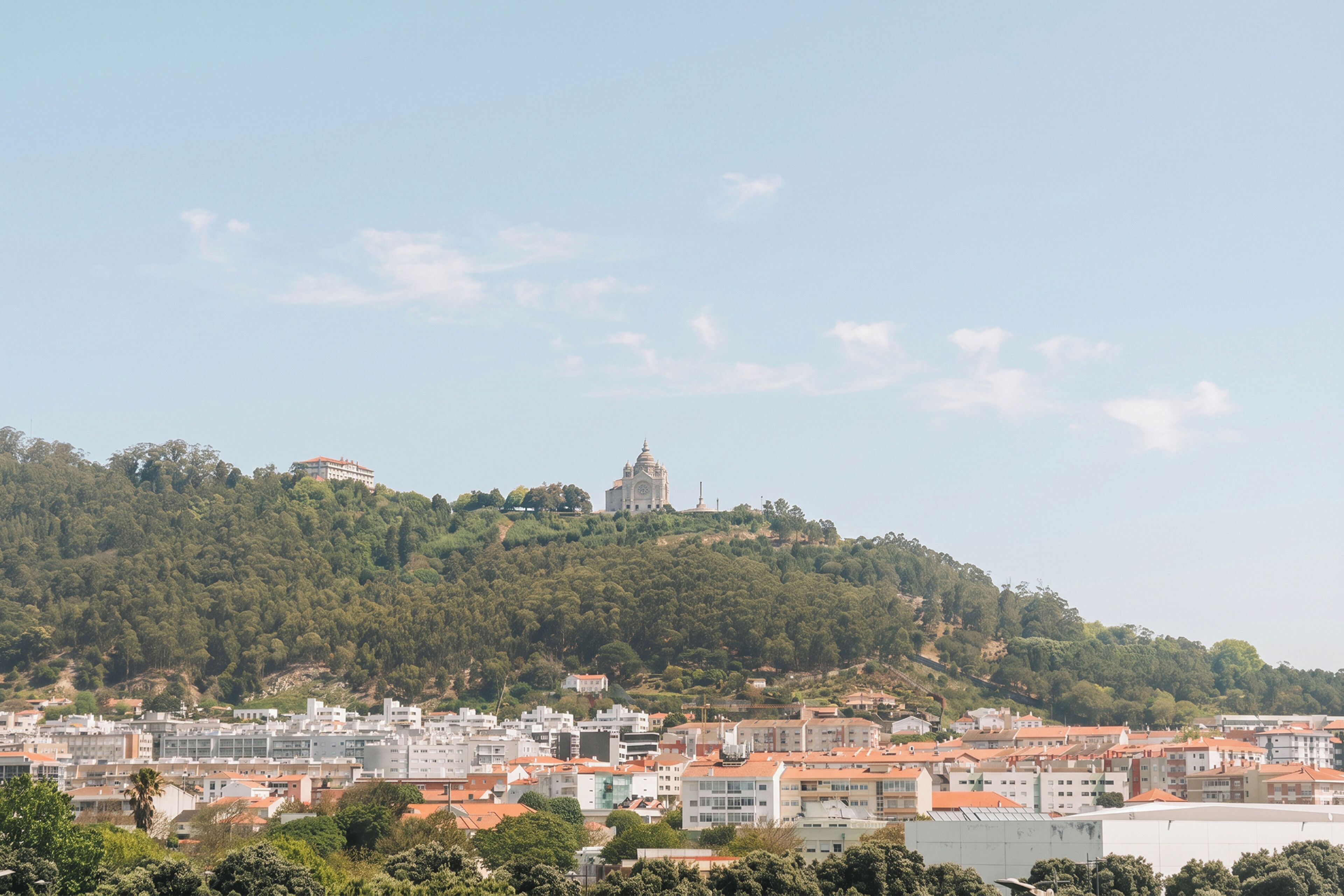 Paisagem urbana com edifícios numa encosta, uma estrutura em cúpula proeminente no topo, e céu claro.