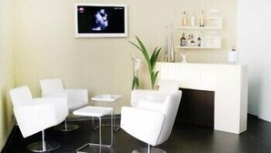 Quarto moderno e minimalista com mobiliário branco, balcão de recepção e tela de televisão.