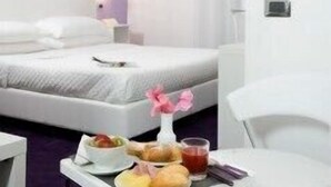 Quarto de hotel com cama, mesa de cabeceira, cadeira e bandeja com itens de café da manhã.