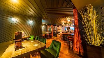 Restaurante com vigas de madeira no teto, cadeiras estofadas em verde e um espaço de bar.