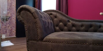Um sofá com capitonê e detalhes dourados em um quarto com parede roxa e um lustre.