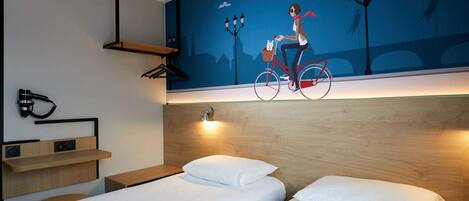 Quarto de hotel com duas camas, cabeceira de madeira, prateleira fixada na parede e um mural com a imagem de uma pessoa de bicicleta.
