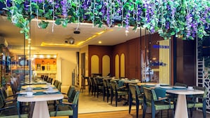 Restaurante com mesas e cadeiras redondas, área de bar e vista para a rua.