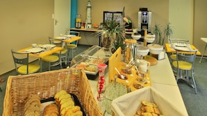 Um quarto com mesas e cadeiras, uma mesa de buffet com pão e pastelaria, um modelo de farol e um dispensador de água.