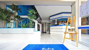 Uma área de recepção com carpete azul com a inscrição 'Entre Terre & Mer', um balcão de atendimento e uma escada de madeira.