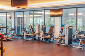 Uma academia com diversos equipamentos de ginástica, grandes janelas e plantas.