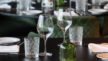 Mesa de jantar posta com diversos copos e taças, incluindo taças de vinho e uma garrafa verde, possivelmente para uma refeição ou evento.