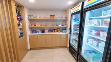 Uma loja com prateleiras cheias de lanches e bebidas, um refrigerador e armários de madeira.