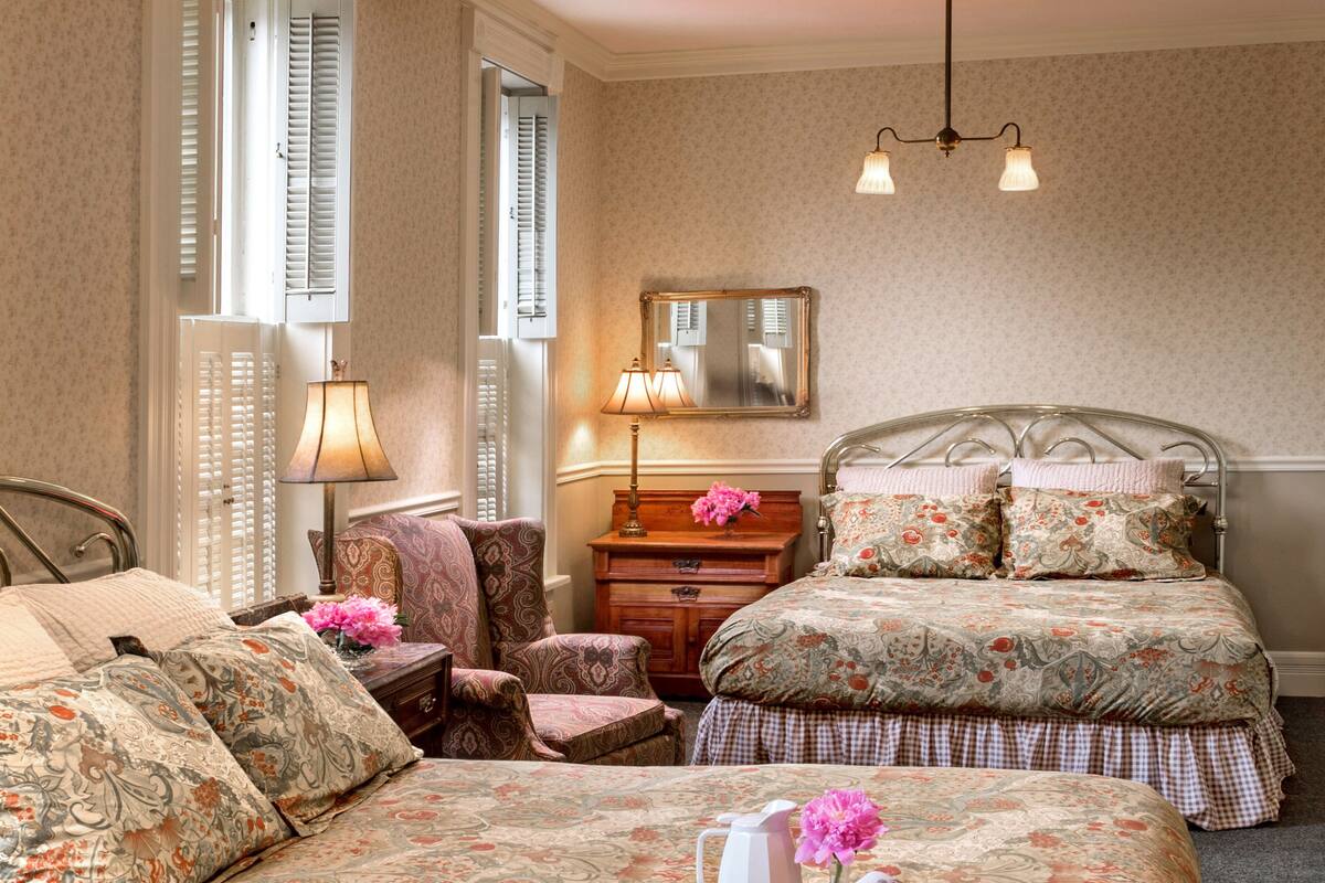 Quarto com duas camas, uma cômoda, uma cadeira e um espelho.