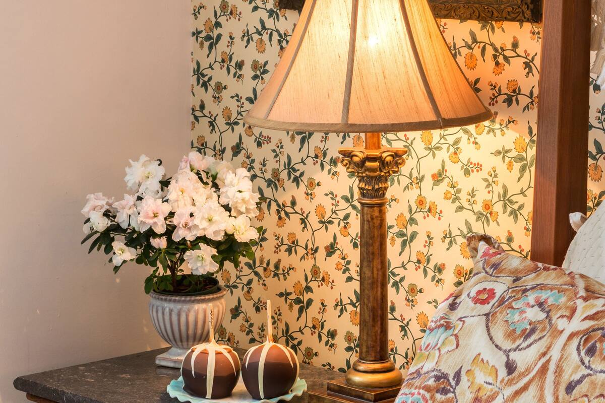 Um recanto aconchegante para leitura, com uma luminária, um livro e um vaso de flores.