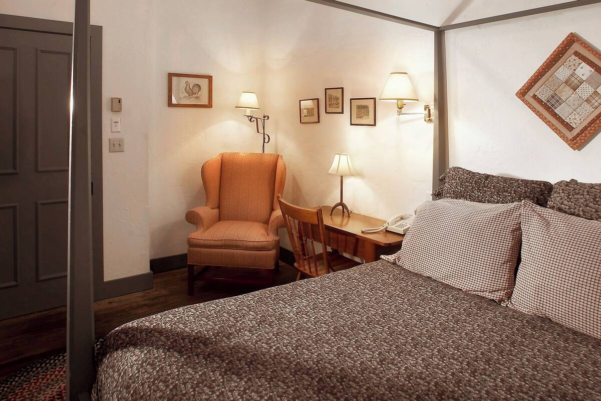 Quarto com cama, cadeira, mesa e luminárias fixadas na parede.