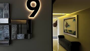 Um corredor com uma grande placa iluminada com o número 9, painéis de parede de mármore, uma obra de arte emoldurada e um banco de cor escura.