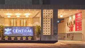 Exterior do Royal Orchid Central em GRAZIA, com uma placa iluminada de destaque, entrada bem iluminada e plantas em vasos na base.