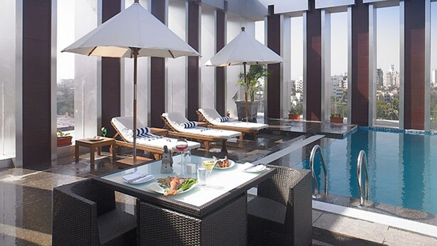 Área de piscina no terraço com espreguiçadeiras, guarda-sóis e uma mesa de jantar com refeição.
