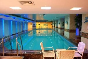 Piscina interior longa com água cristalina, rodeada por paredes com elementos decorativos e algumas cadeiras de descanso.