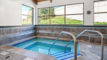 Piscina com água azul cristalina, rodeada por azulejos de pedra e uma bordadura em azulejos.