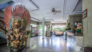 Um hall amplo com uma grande estátua, um balcão de recepção e uma escadaria.