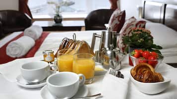Mesa de café da manhã com cama, almofadas, um vaso com flores, uma fruteira, uma cafeteira e um frasco de mel.