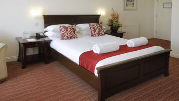 Quarto de hotel com cama grande, mesa de cabeceira com telefone e placa, radiador e porta.