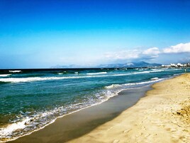 Uma praia com ondas, céu claro e montanhas ao longe.