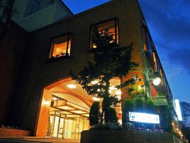 Entrada de hotel com fachada de tijolos, uma grande porta em arco e sinalização indicando área de estacionamento.