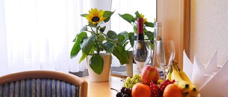 Quarto de hotel com escrivaninha de madeira, planta em vaso, garrafa de vinho, taças de vinho e bandeja de frutas.