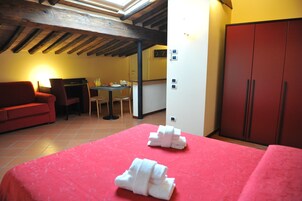 Quarto de hotel com cama, um sofá vermelho, uma mesa de jantar com cadeiras e um guarda-roupa.