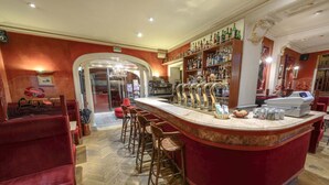 Uma área de bar com balcão vermelho, vários bancos e uma variedade de garrafas nas prateleiras.