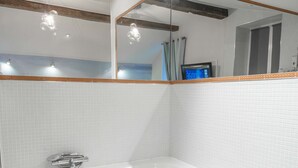 Uma casa de banho moderna com uma banheira independente, um espelho grande e um relógio digital.
