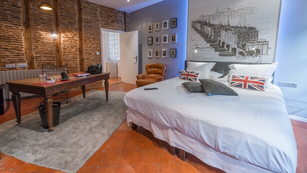 Quarto com cama, escrivaninha, cadeira e parede decorada com quadros.